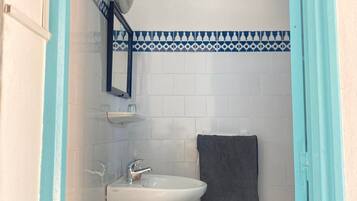 Uma casa de banho pequena com uma pia branca, um espelho e um contentor de lixo azul.