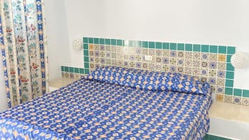 Quarto com cama, cortinas, quadro na parede e cabeceira revestida em azulejo.