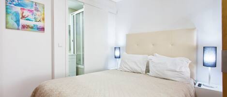 Quarto com cama, luminárias de cabeceira, uma porta e um quadro pendurado na parede.