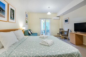 Quarto de hotel com cama, escrivaninha, televisão e varanda com vista.