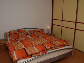 Uma cama com um cobertor laranja e bege estampado, uma mesa de cabeceira com abajur e uma cabeceira de madeira.
