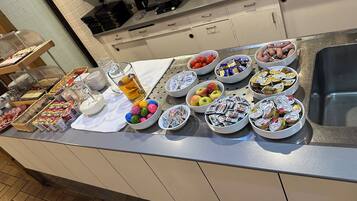 Mesa de buffet com diversos alimentos e um copo de líquido âmbar.