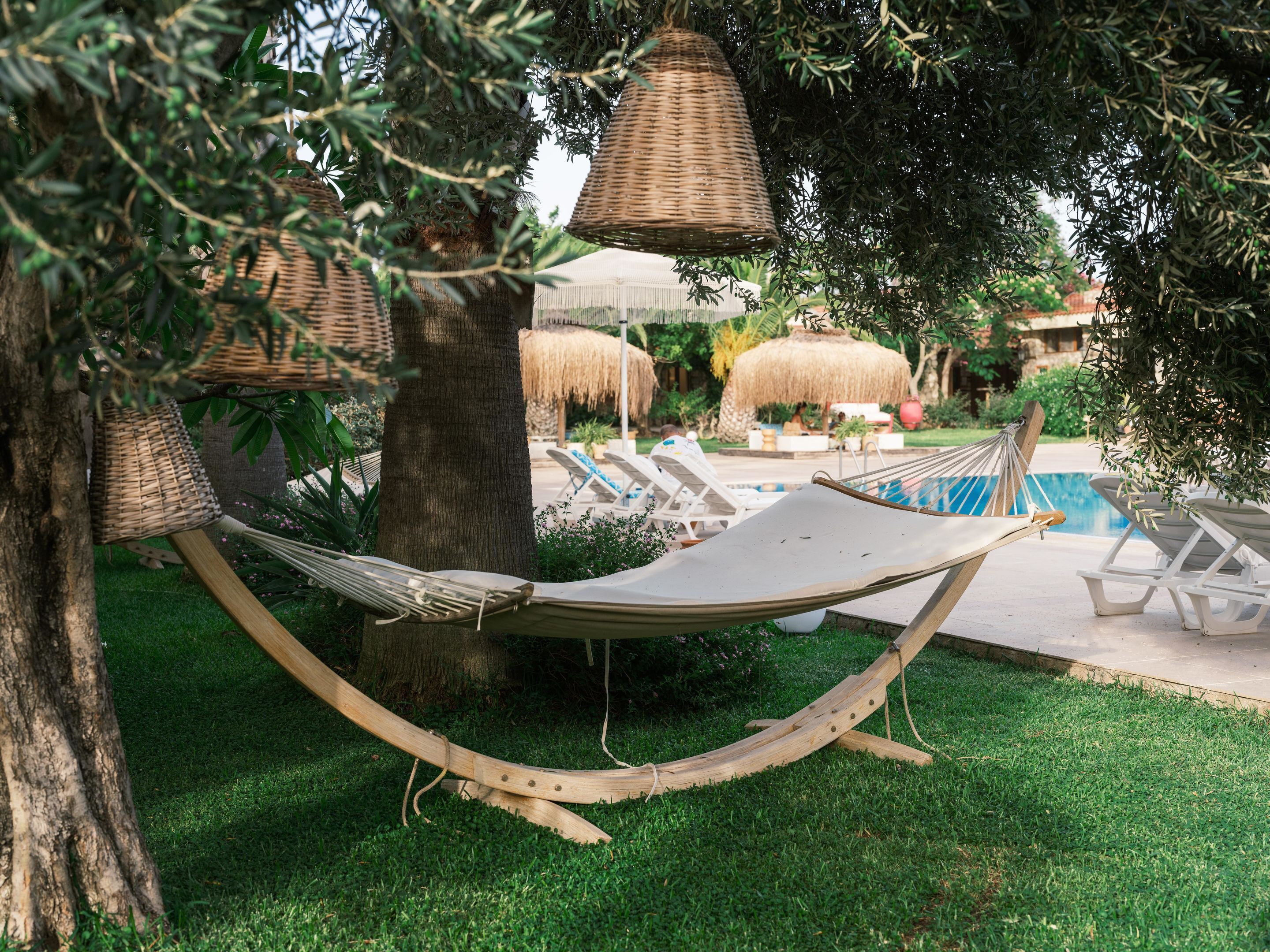 Uma rede sob uma árvore, uma piscina e cadeiras de descanso.