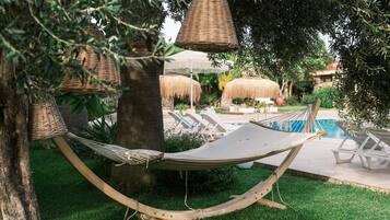 Uma rede sob uma árvore, uma piscina e cadeiras de descanso.