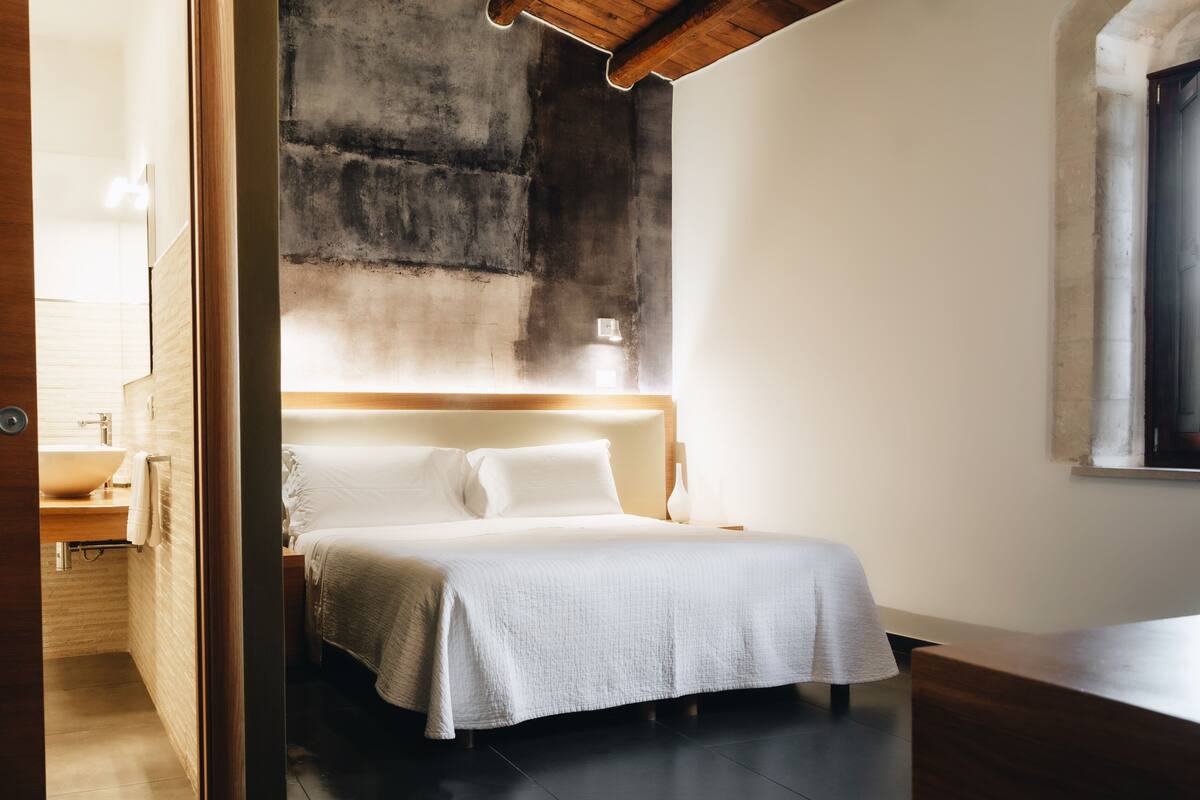 Quarto moderno com cabeceira de madeira, mesa de cabeceira e uma janela grande.
