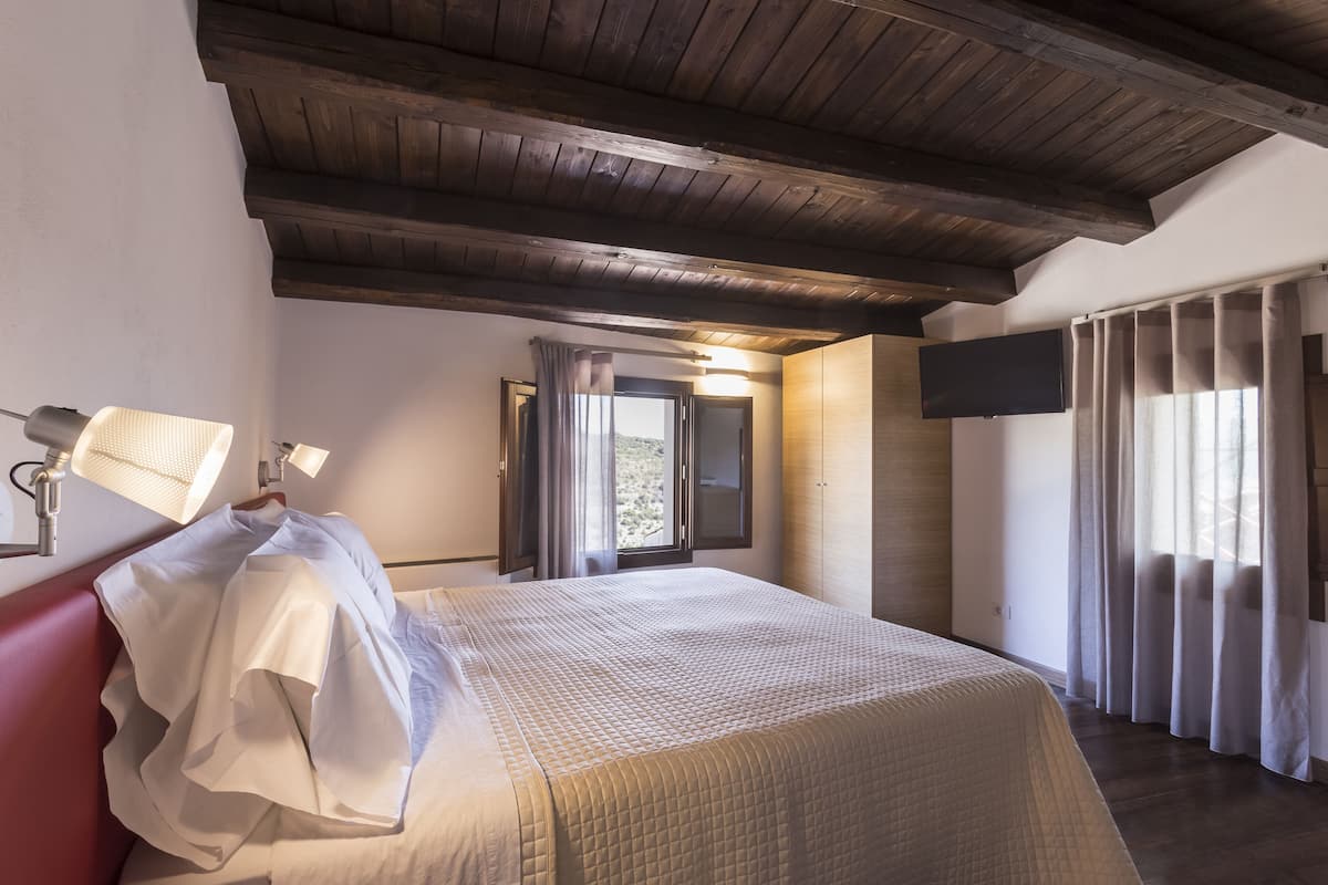 Quarto com cama grande, teto de madeira, televisão de tela plana e janela com cortinas.