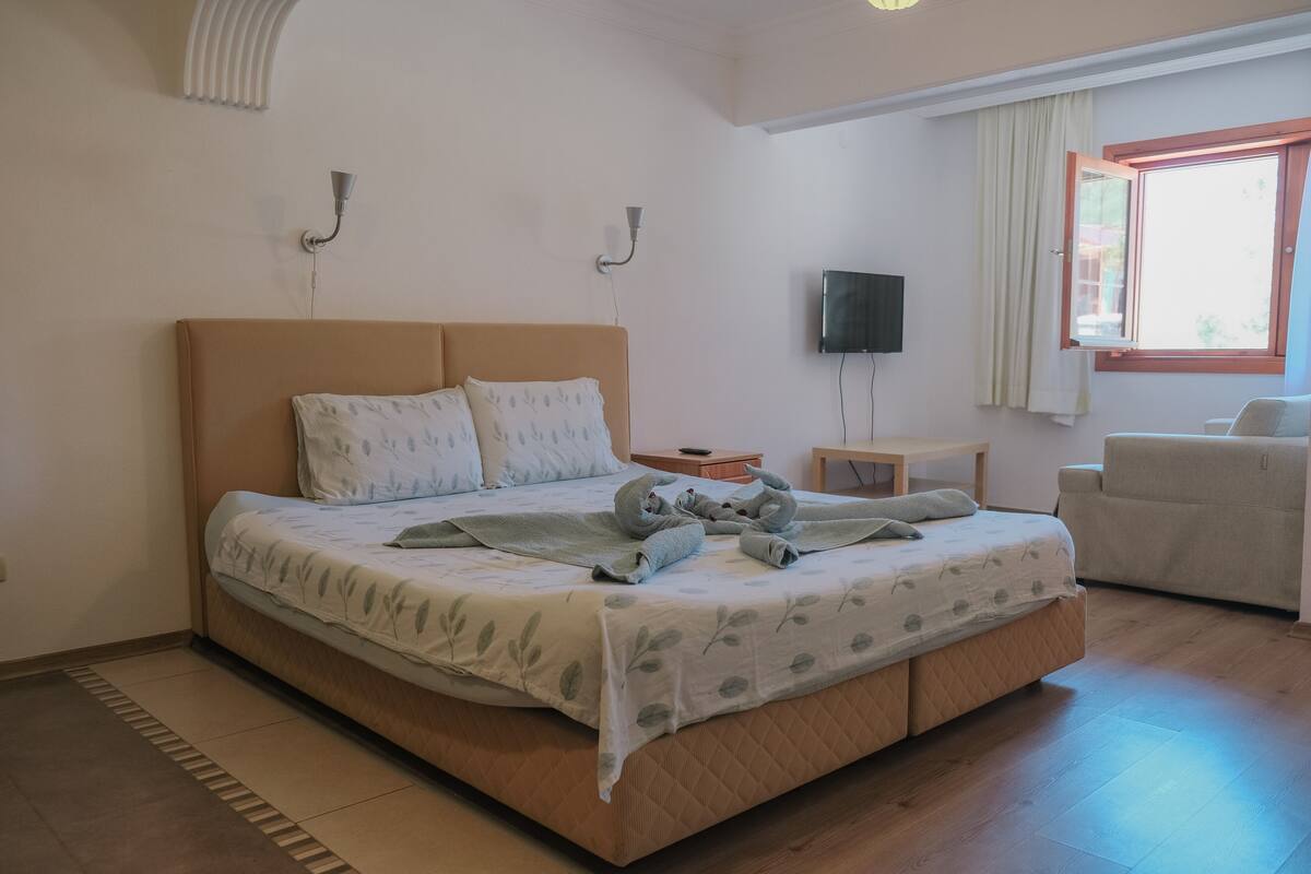 Quarto com cama, mesa de cabeceira, televisão e janela com cortinas.