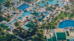 Vista aérea de um resort com várias piscinas, palmeiras e áreas de descanso.