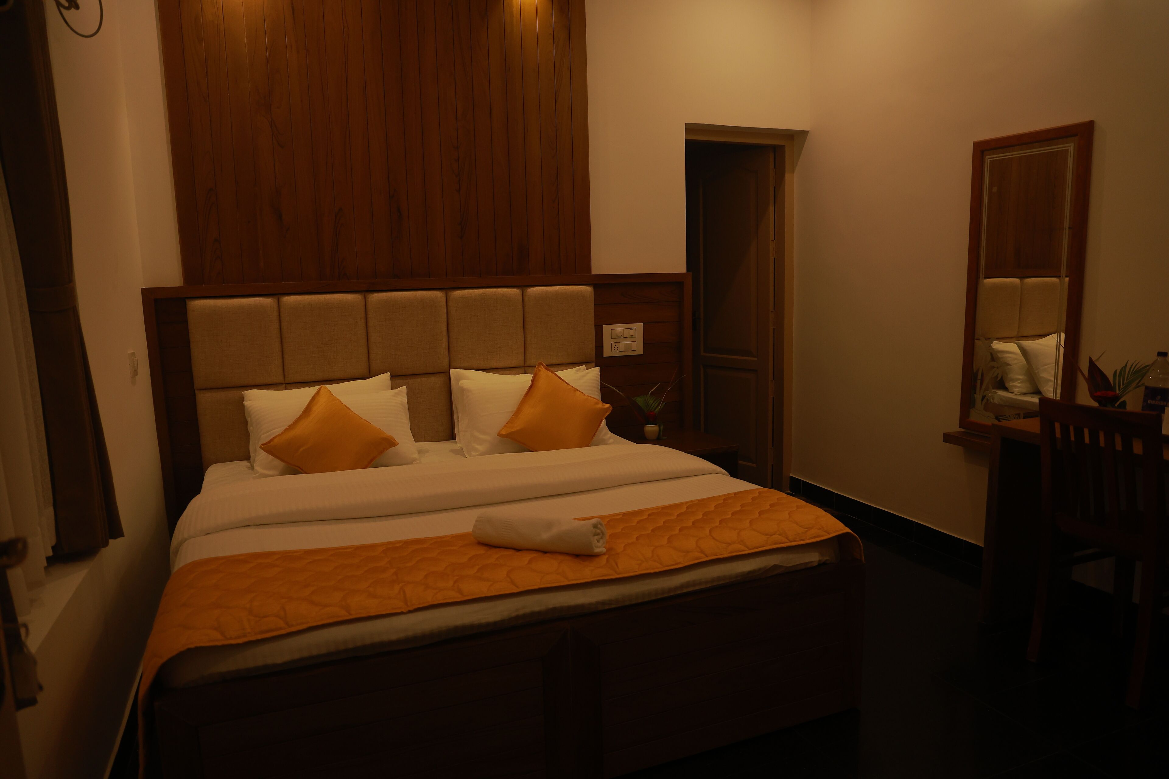Cama bem arrumada com cabeceira, mesa de cabeceira de madeira, uma cadeira e um espelho.