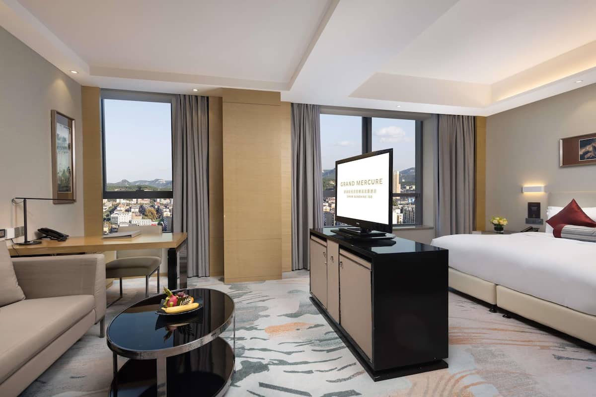 Quarto de hotel com cama, escrivaninha, televisão e vista para a cidade.