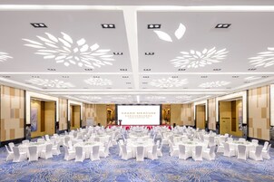 Uma sala de conferência com mesas redondas, cadeiras brancas e uma tela grande exibindo "GRAND MERCURY".