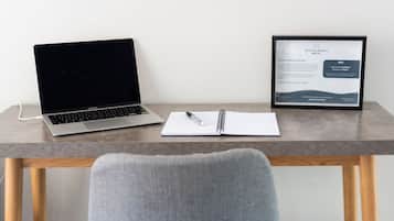 Um laptop numa secretária com um caderno e caneta, e um letreiro de boas-vindas emoldurado para o Raglan Sunset Motel.