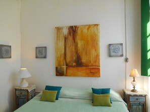 Quarto com cama, duas almofadas, uma obra de arte na parede e duas mesas de cabeceira com luminárias.