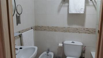 Casa de banho com sanita, bidé, lavatório e uma toalha pendurada na parede.