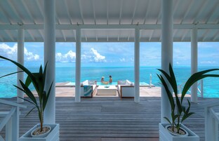 Área externa coberta com piscina, duas pessoas relaxando e vista para o oceano.