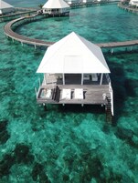Uma cabana sobre a água com telhado branco, deck de madeira e espreguiçadeiras.