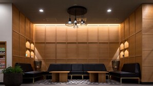 Um lobby moderno com um sofá preto, painéis de madeira e iluminação pendente.