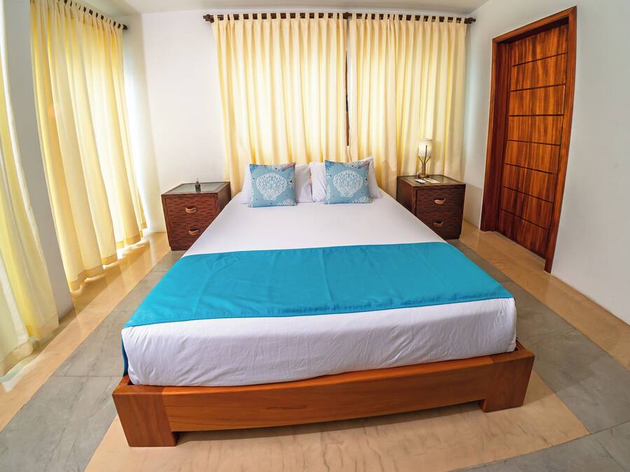 Uma cama grande com colcha azul e branca, duas almofadas combinando, cabeceiras de madeira e um guarda-roupa de madeira.