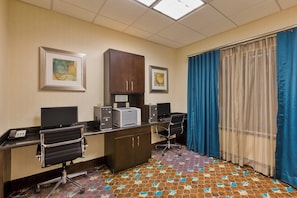 Quarto de hotel com escrivaninha, duas cadeiras, computador, impressora e telefone.