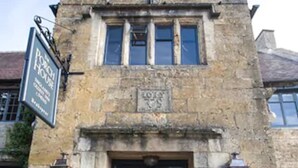 Um edifício de pedra com porta de entrada escura, uma placa de identificação acima da porta e uma pequena janela.