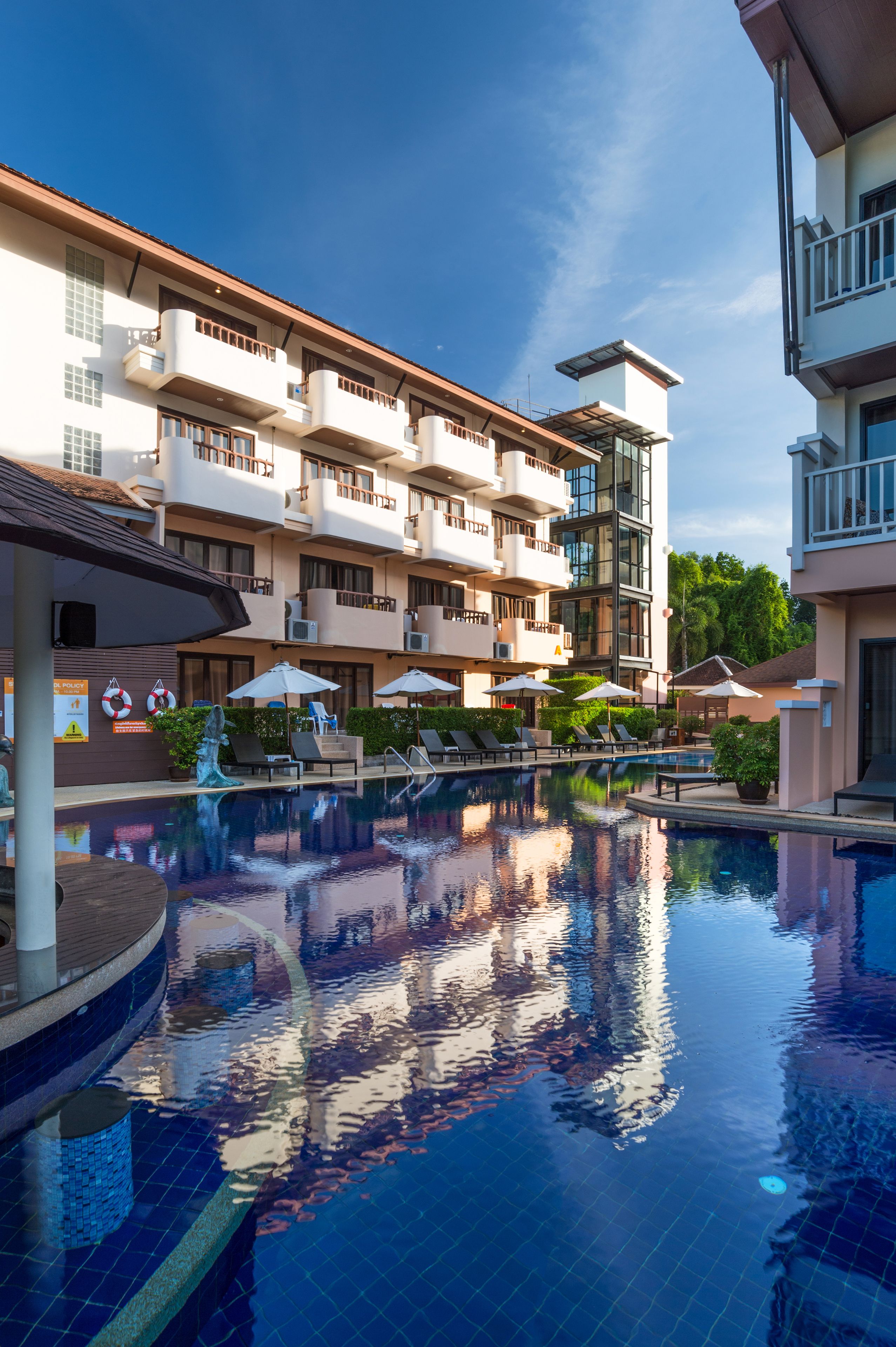 Um hotel com piscina, várias varandas e guarda-sóis.