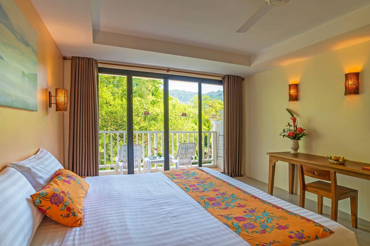 Quarto de hotel com cama, escrivaninha e varanda com vista para o verde.
