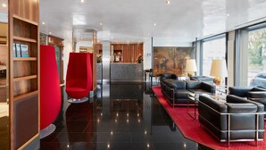 Um hall moderno com balcão de recepção, área de estar e uma parede com detalhes em vermelho.
