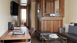 Quarto de hotel moderno com piso de madeira, mesa de centro de vidro, sofá de couro, escrivaninha de madeira e televisão de tela plana fixada na parede.