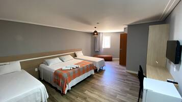 Quarto de hotel com duas camas de solteiro, um banco, uma mesinha, uma televisão e um frigorífico.
