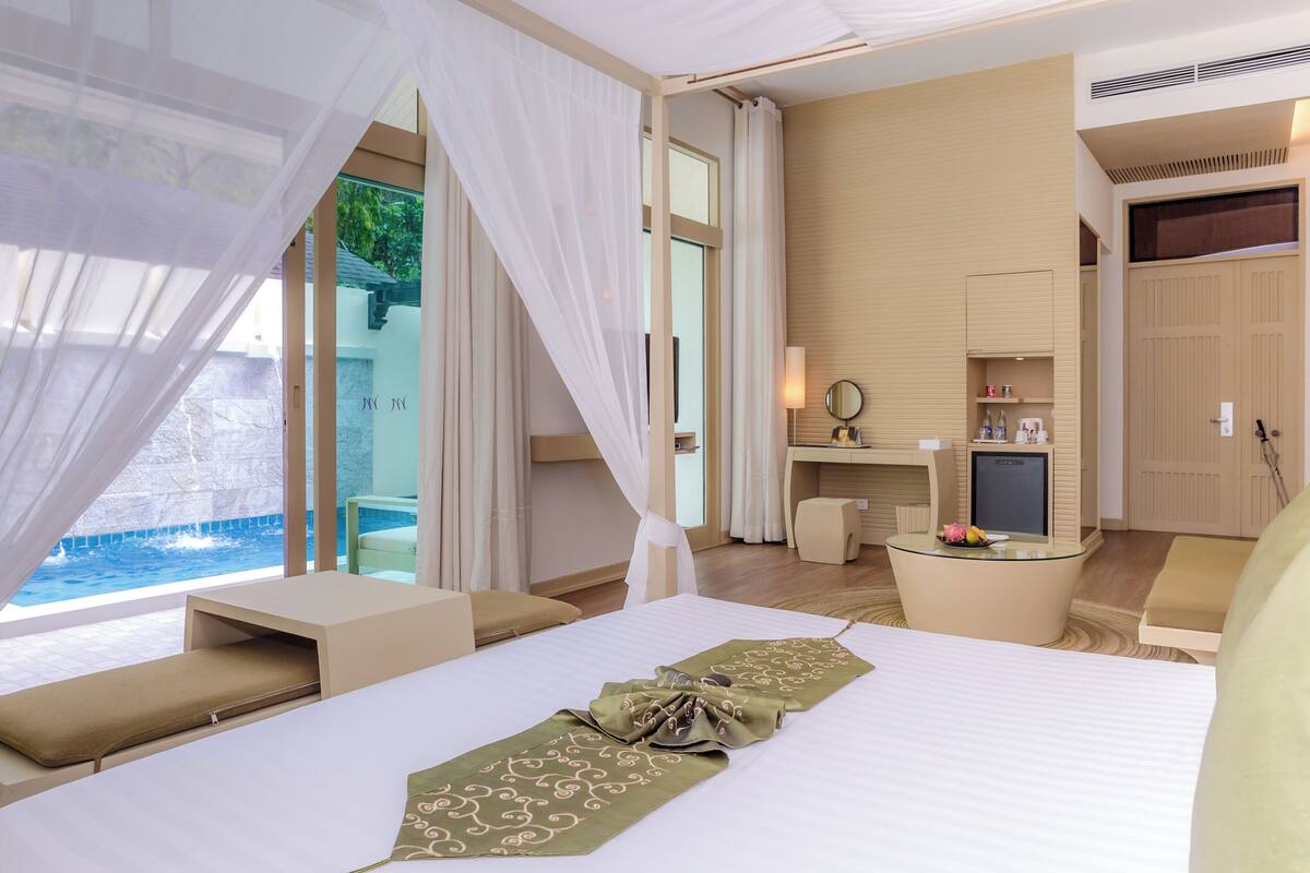 Quarto de hotel moderno com uma cama grande, área de estar, escrivaninha e vista para uma piscina.
