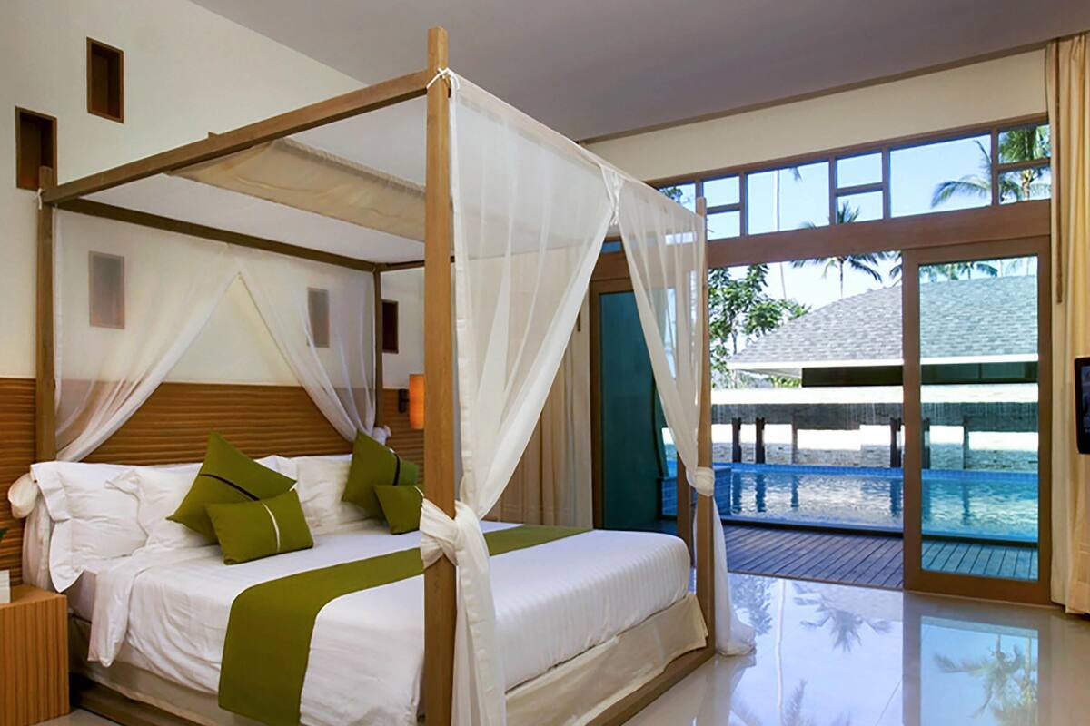 Uma cama com dossel, cabeceira de madeira e almofadas verdes.