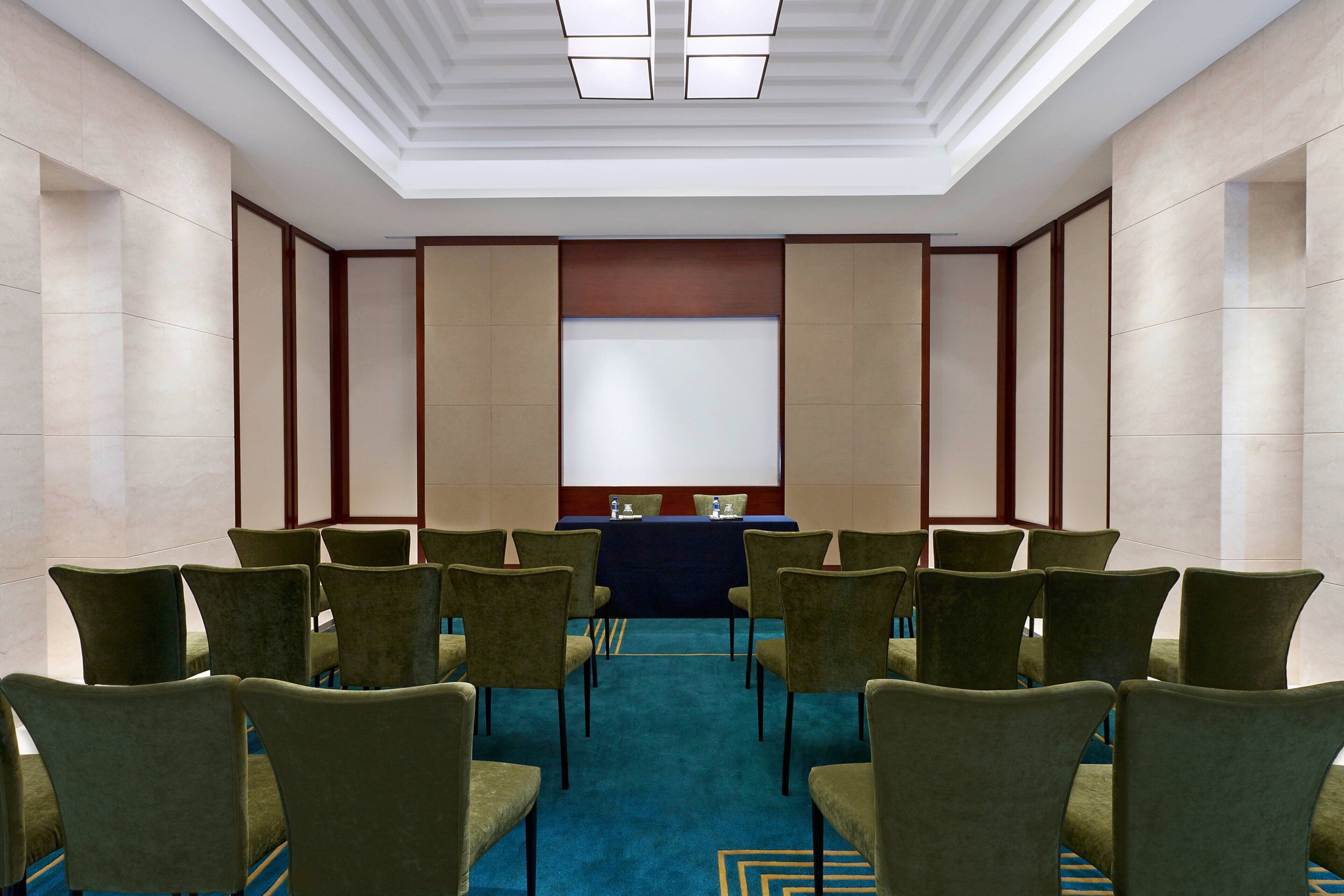 Uma sala de conferências com uma mesa comprida, cadeiras e uma tela na frente.