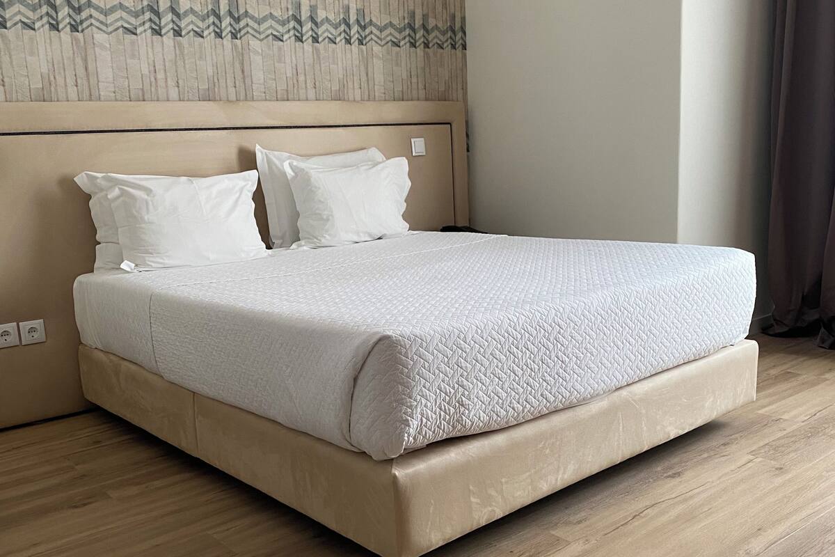Quarto de hotel moderno com uma cama grande, piso de madeira e parede estampada.