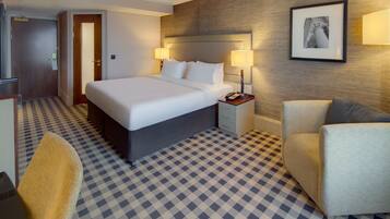 Quarto de hotel com piso xadrez, cama com roupa de cama branca, duas luminárias de cabeceira, mesa de cabeceira com telefone e quadro na parede.