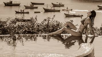 Uma mulher relaxando à beira da piscina, com barcos ao fundo.