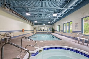 Uma piscina com borda azulejada, uma banheira de hidromassagem e um teto com vigas aparentes e luminárias.