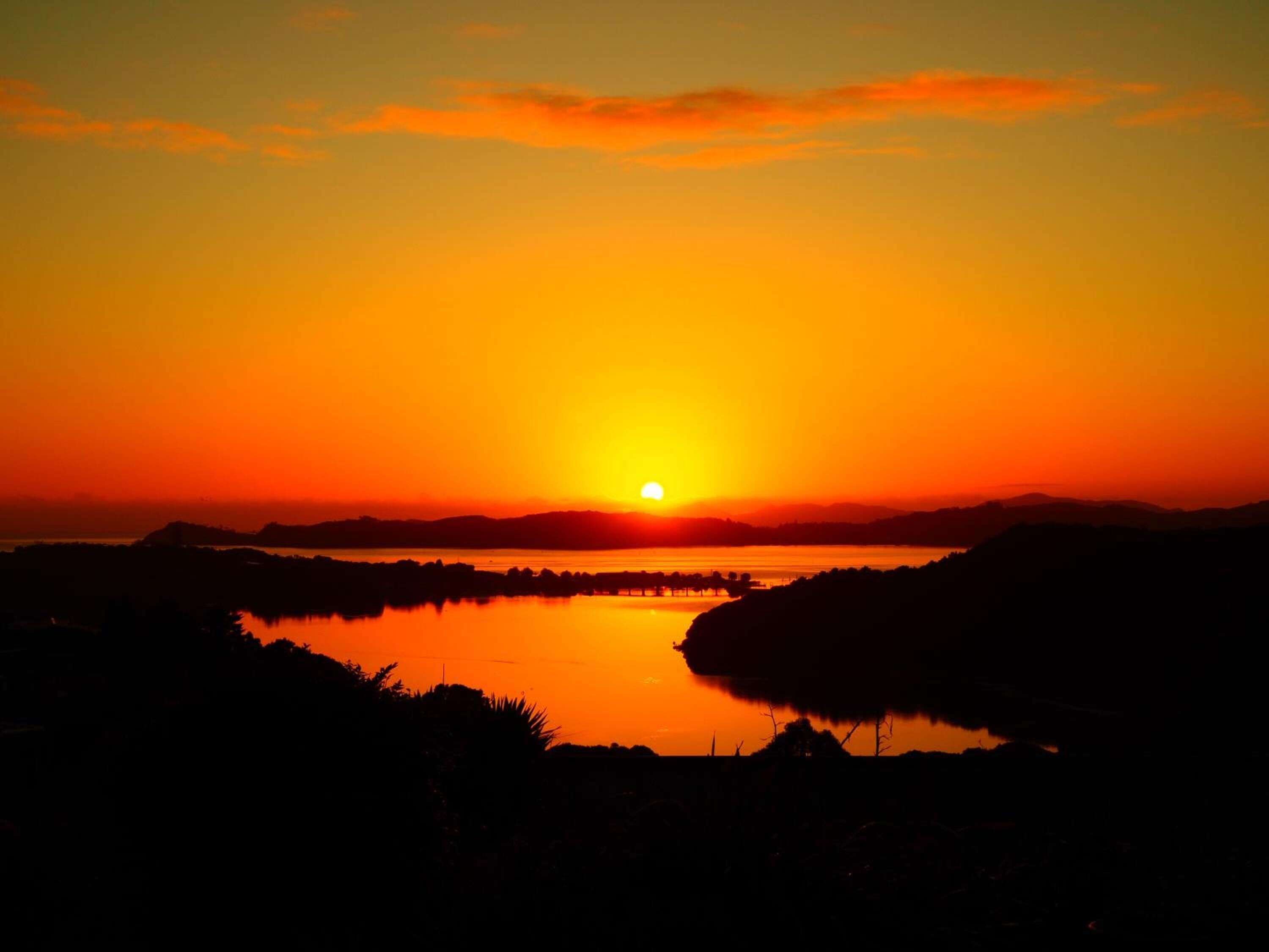 Pôr do sol sobre um lago, com o perfil de colinas ao fundo.
