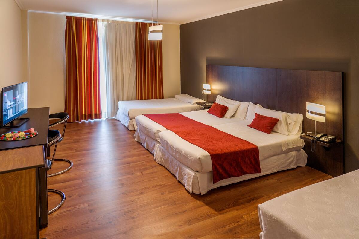 Quarto de hotel com duas camas, uma mesa de trabalho com um laptop e uma televisão.