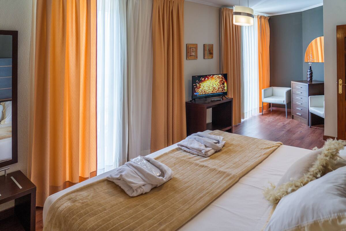 Quarto de hotel com uma cama, uma escrivaninha com televisão, uma cadeira e um armário.