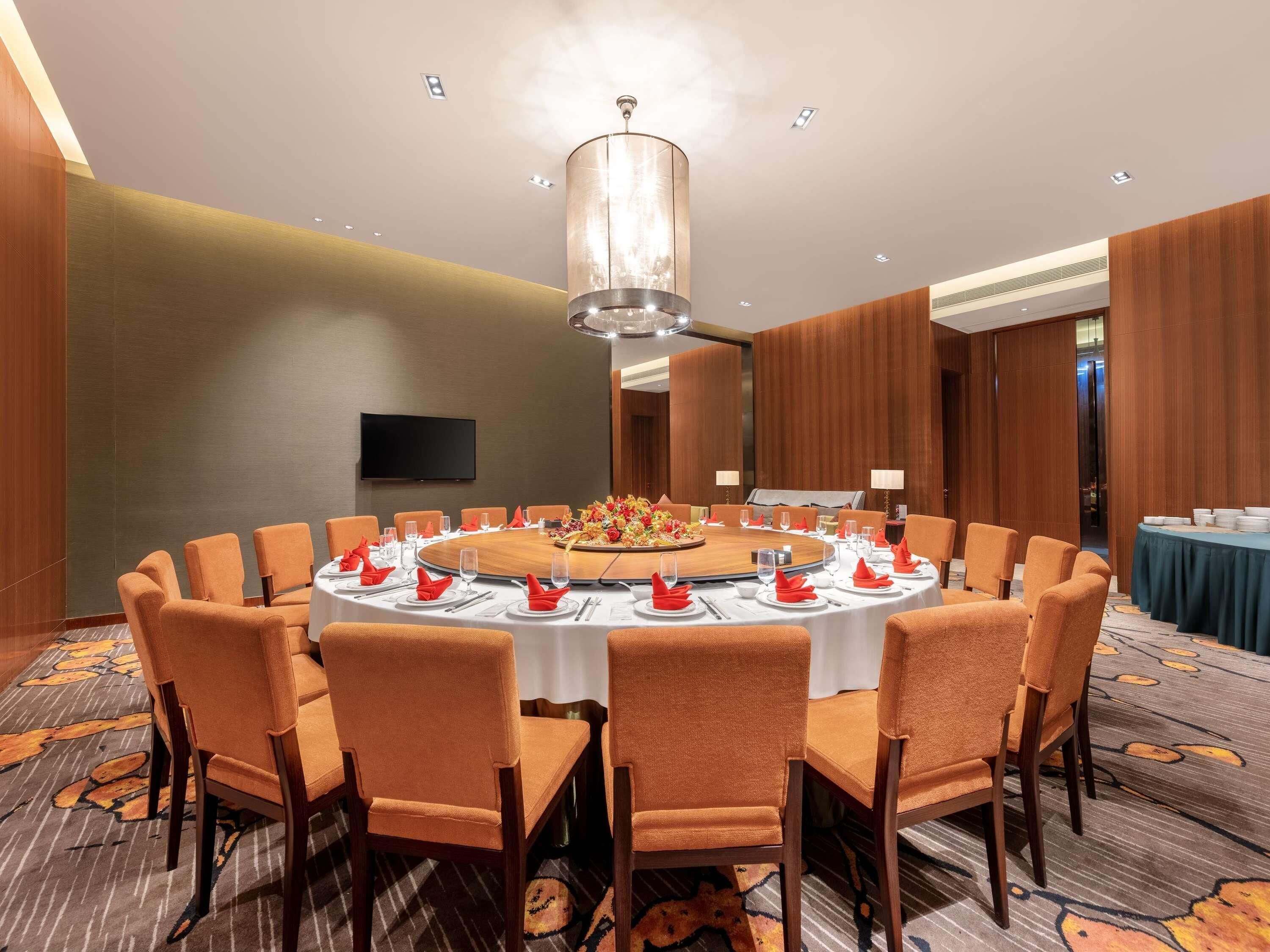 Uma sala de conferências com uma mesa redonda, cadeiras laranja, toalhas de mesa brancas e um candelabro.
