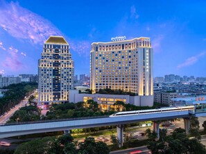Um hotel moderno e alto com um letreiro grande da Pullman, cercado por um horizonte urbano e um trem passando acima.