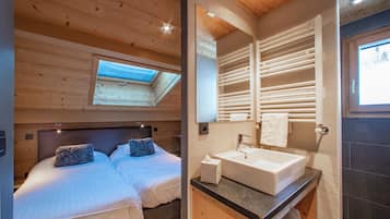 Quarto com duas camas, um claraboia e banheiro com uma pia grande e espelho.