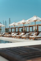 Área da piscina com espreguiçadeiras de madeira e guarda-sóis brancos.