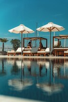 Área da piscina com espreguiçadeiras e guarda-sóis, um deck de madeira e céu azul.