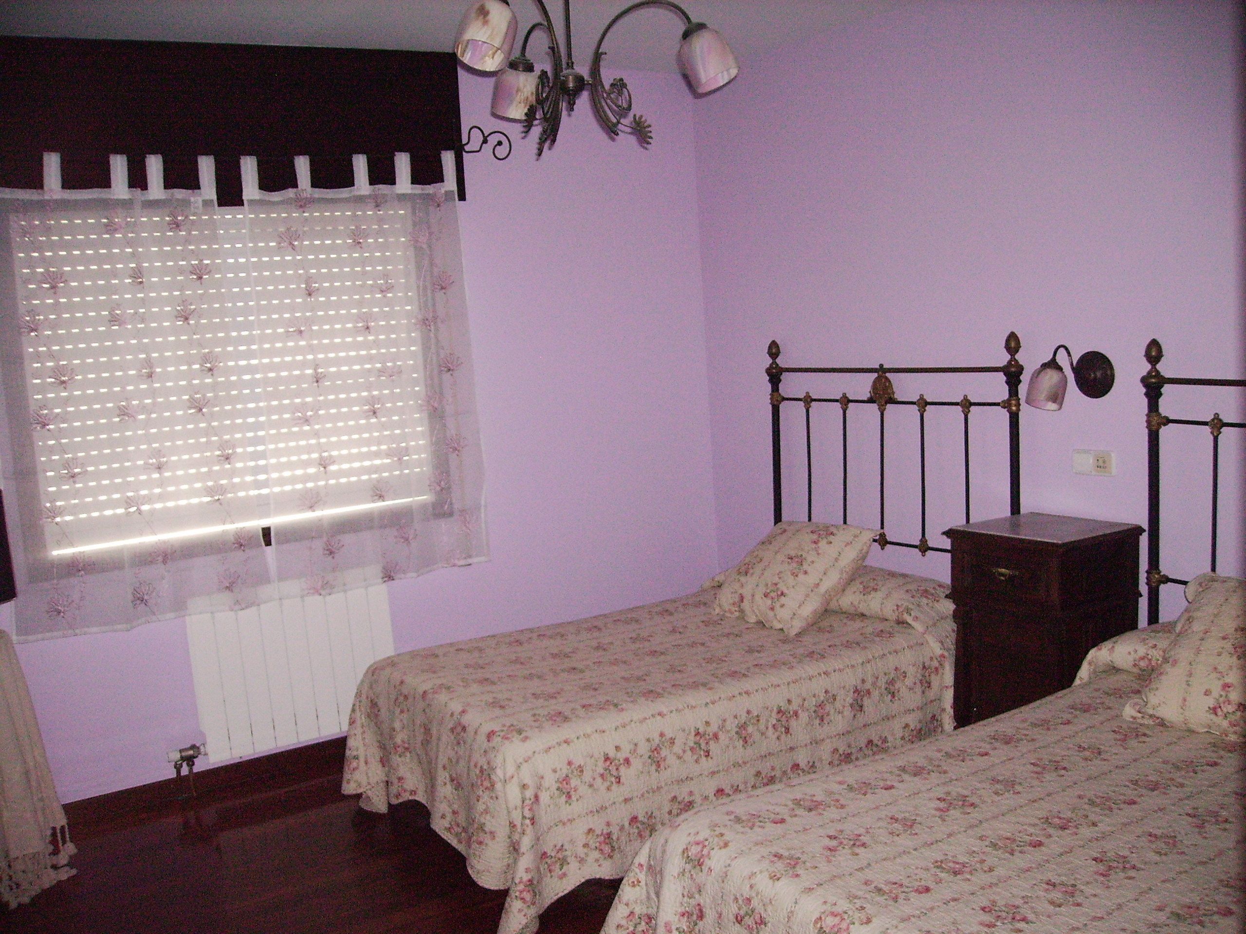 Quarto com duas camas de solteiro, mesa de cabeceira, luminária e janela com persianas.
