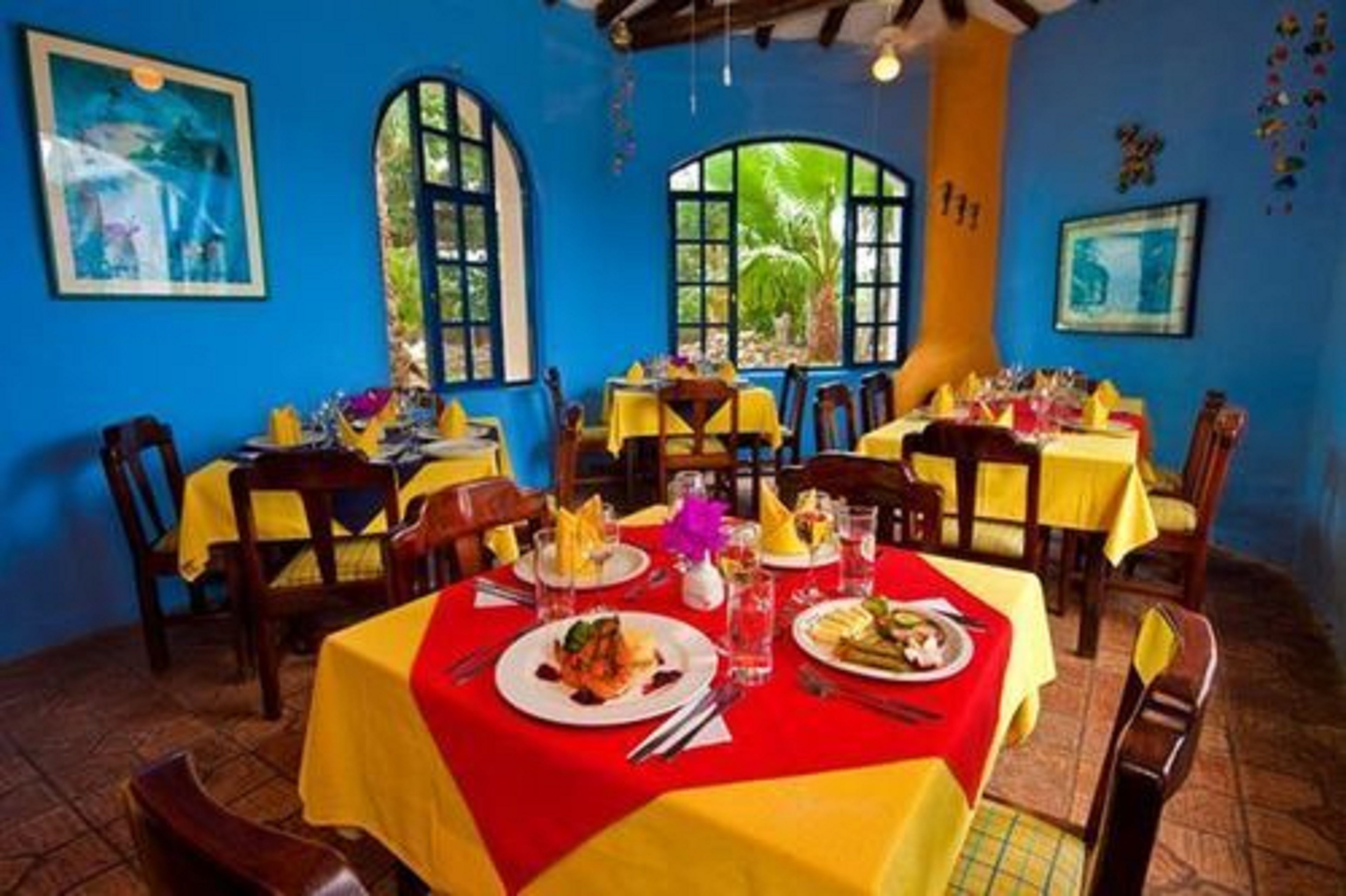 Restaurante com mesas postas para refeições, com toalhas de mesa amarelas e centros de mesa vermelhos.