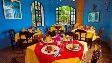 Restaurante com mesas postas para refeições, com toalhas de mesa amarelas e centros de mesa vermelhos.