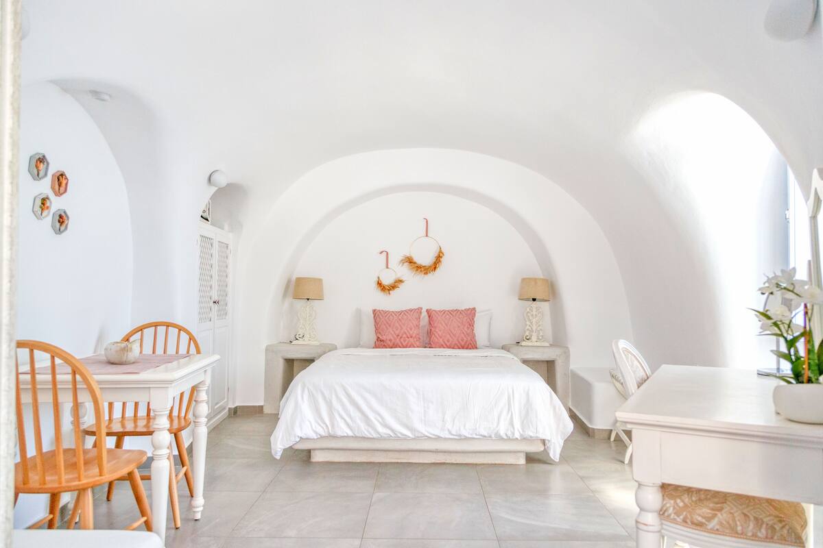 Quarto com cama branca, duas mesas de cabeceira, escrivaninha e cadeiras.
