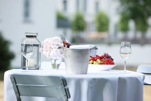 Uma mesa posta com uma taça de vinho, uma vela, um vaso de flores, um balde e uma cesta de frutas.