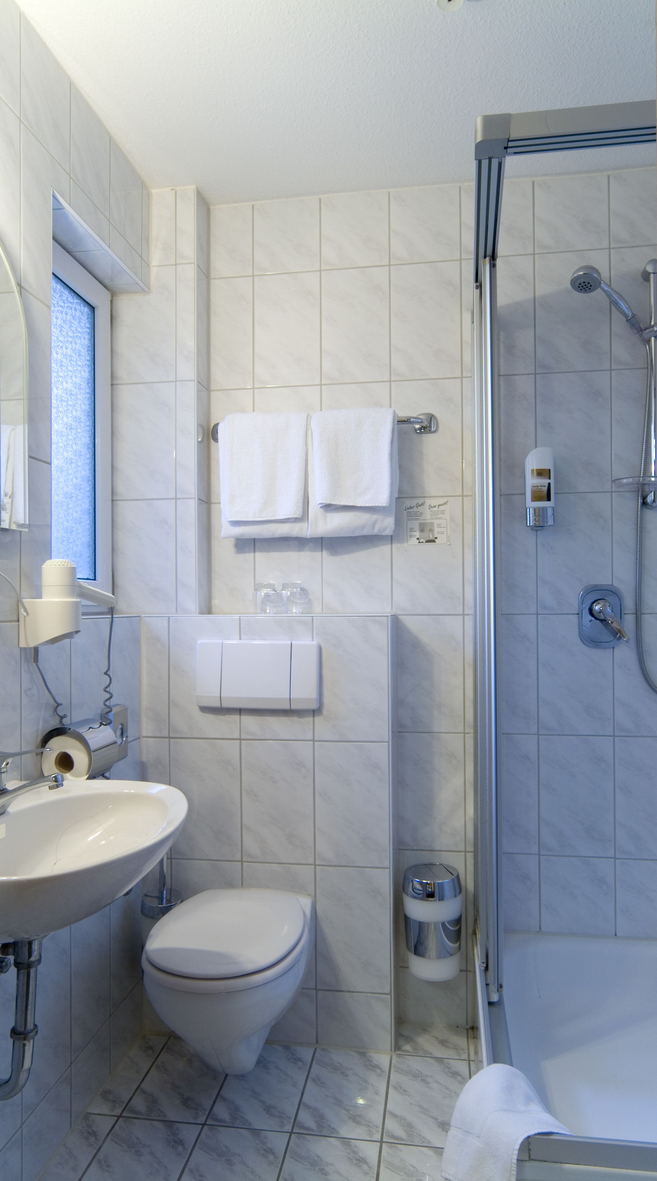Uma casa de banho moderna com chuveiro, sanita, lavatório e suporte para toalhas.